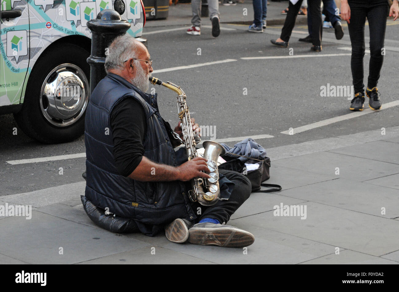 London, UK, 21/08/2015, Saxophone busker sits on the pavement playing ...