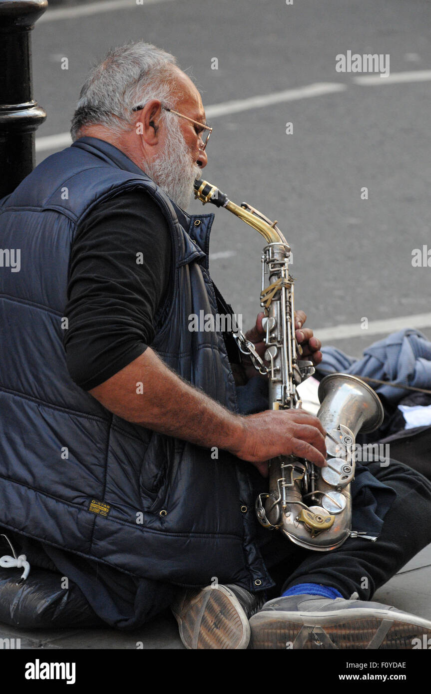 London, UK, 21/08/2015, Saxophone busker sits on the pavement playing ...