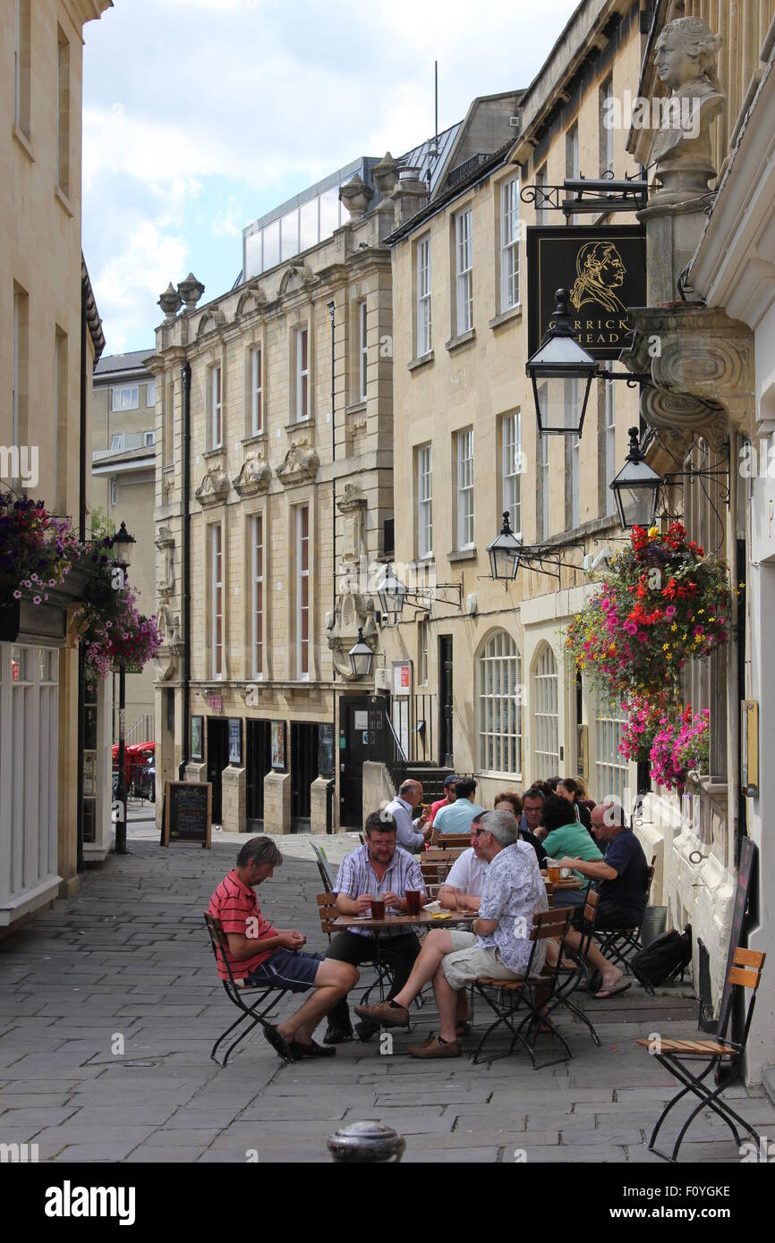 People sitting at tables outside pub on street during summer in Bath ...