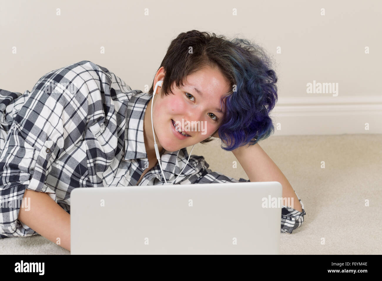 Happy teen girl, looking forward, on computer while listening to music ...
