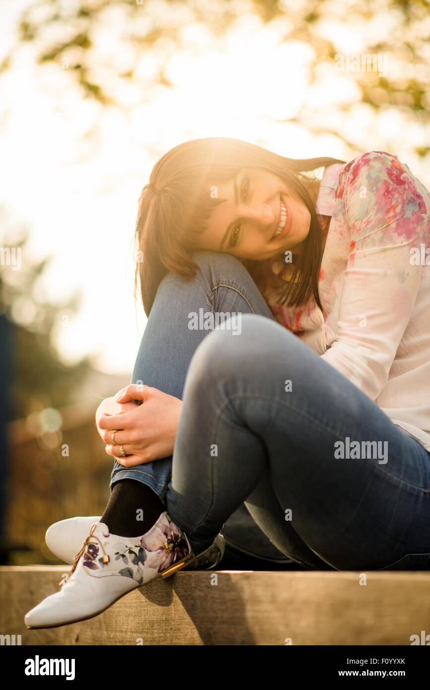 Portrait of woman leaning on her knee sitting outdoor at sunset Stock ...