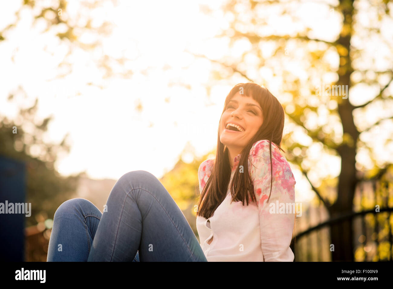 Young woman sitting outdoor and enjoying life with sun in background ...