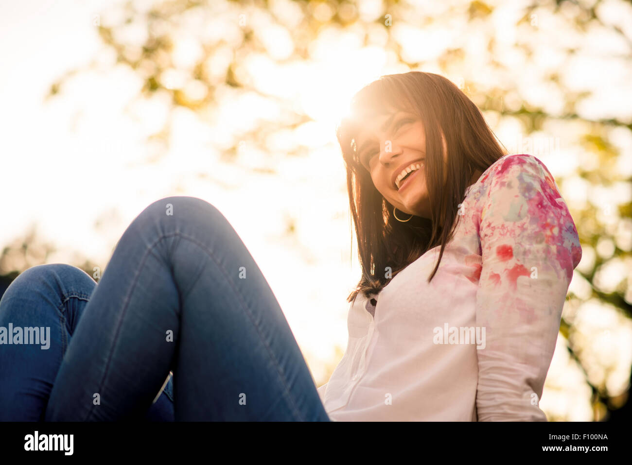 Young woman sitting outdoor and enjoying life with sun in background ...