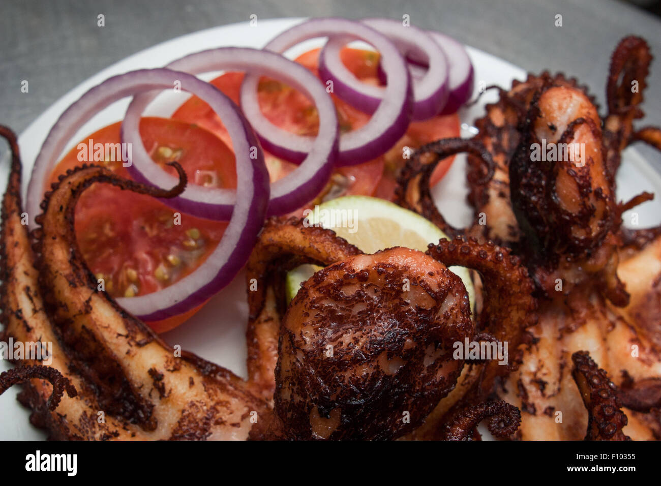 fried octopus served with tomatoes and onion Stock Photo - Alamy