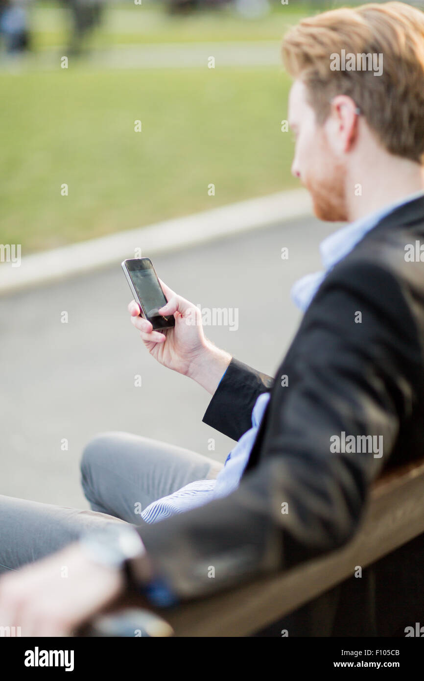 Businessman holding his cell phone while sitting on a park bench Stock ...