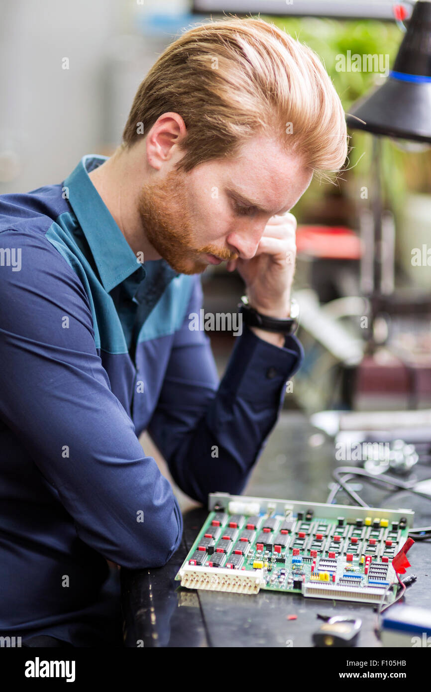 Young handsome man thinking while soldering a circuit board and working ...
