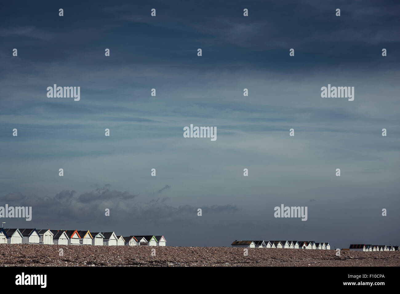 Row of beach huts on a shingle beach are lit by the Spring sunshine in ...