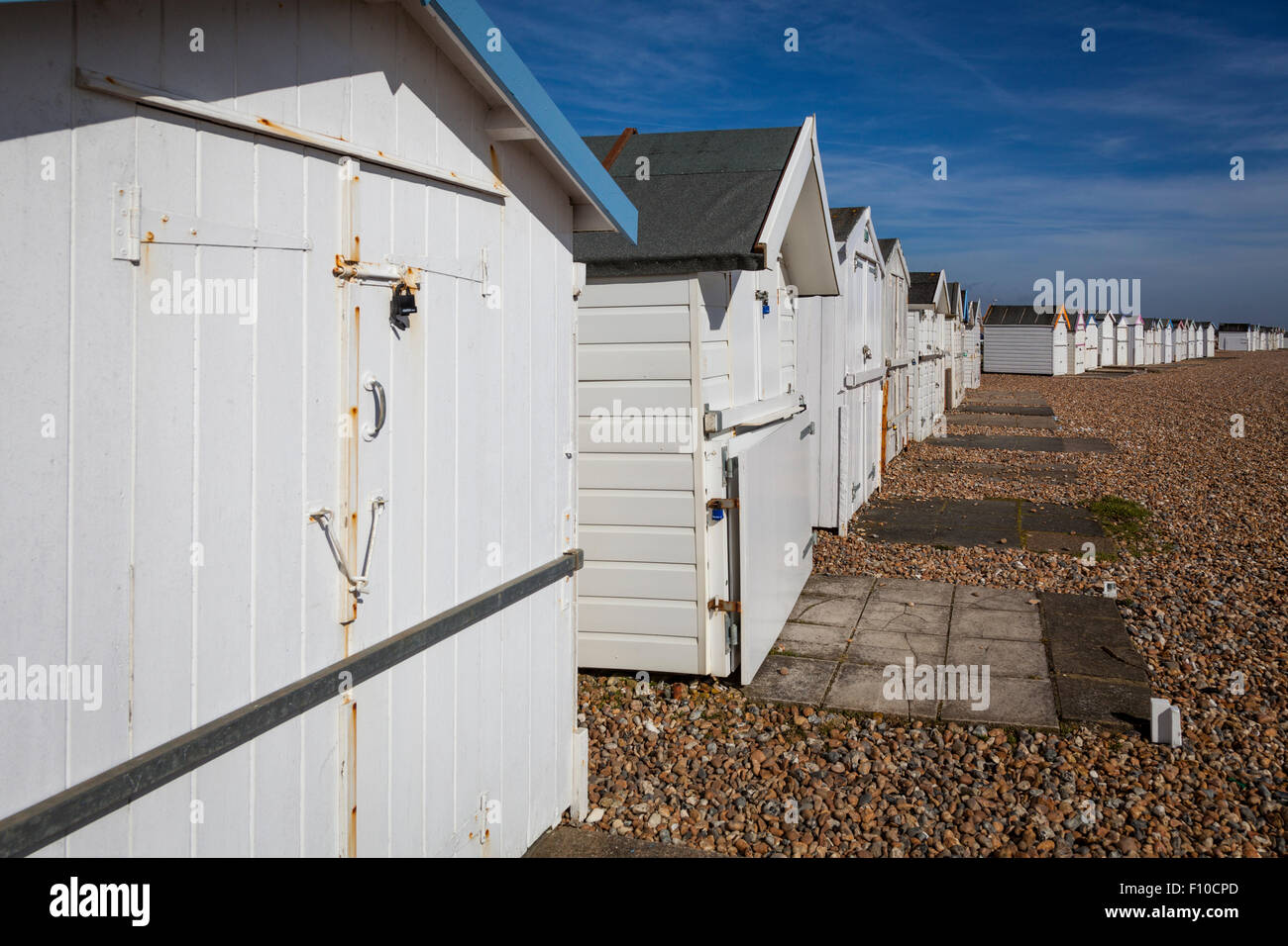 Row of beach huts on a shingle beach are lit by the Spring sunshine in ...
