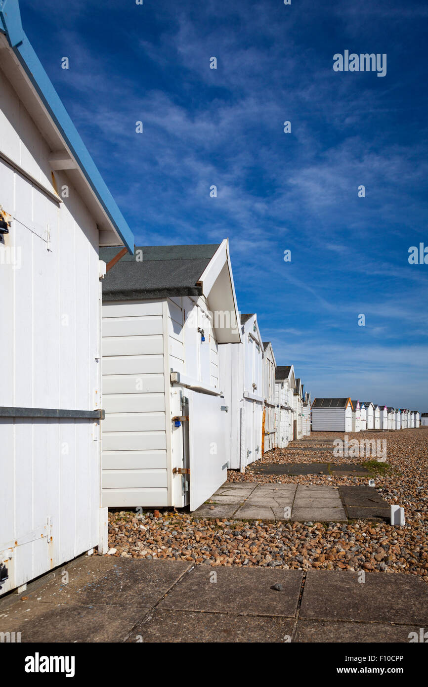 Row of beach huts on a shingle beach are lit by the Spring sunshine in ...