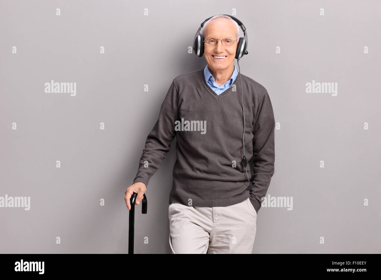 Senior gentleman with a cane listening music on headphones and posing ...