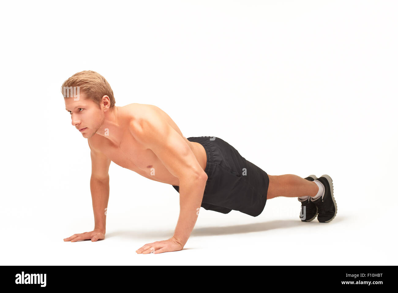 Muscular shirtless sportsman making push-ups on palms in studio with ...