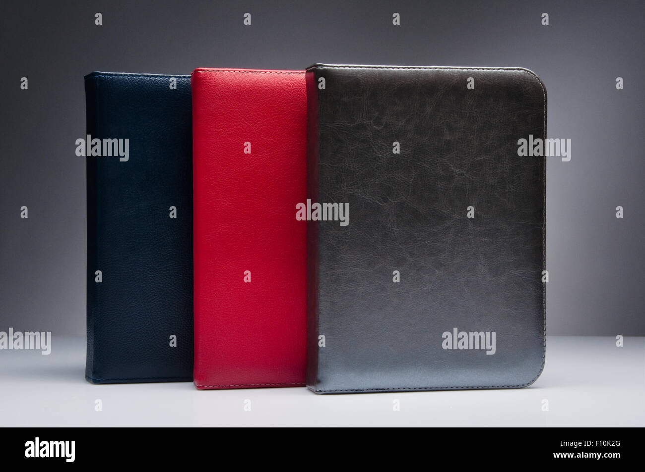 Three notebooks with natural leather covers of blue, red and gold ...