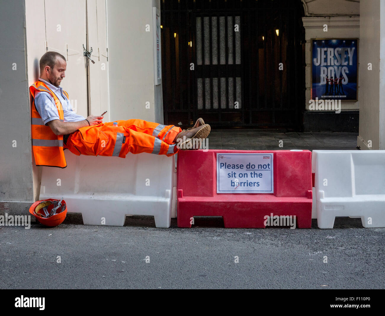 A man sitting on some barriers above a sign that says Please do NOT sit ...