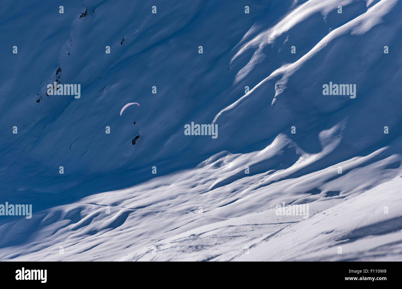 A paraglider is flying high up in the snow covered mountains above a ...