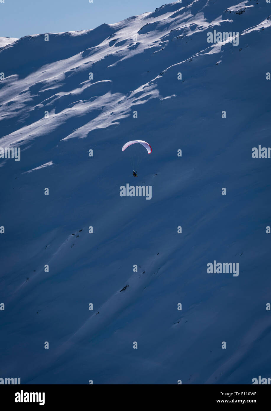 A paraglider is flying high up in the snow covered mountains above a ...