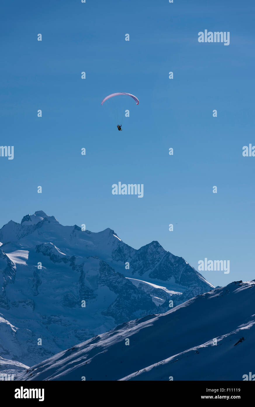 A paraglider is flying high up in the snow covered mountains above the ...