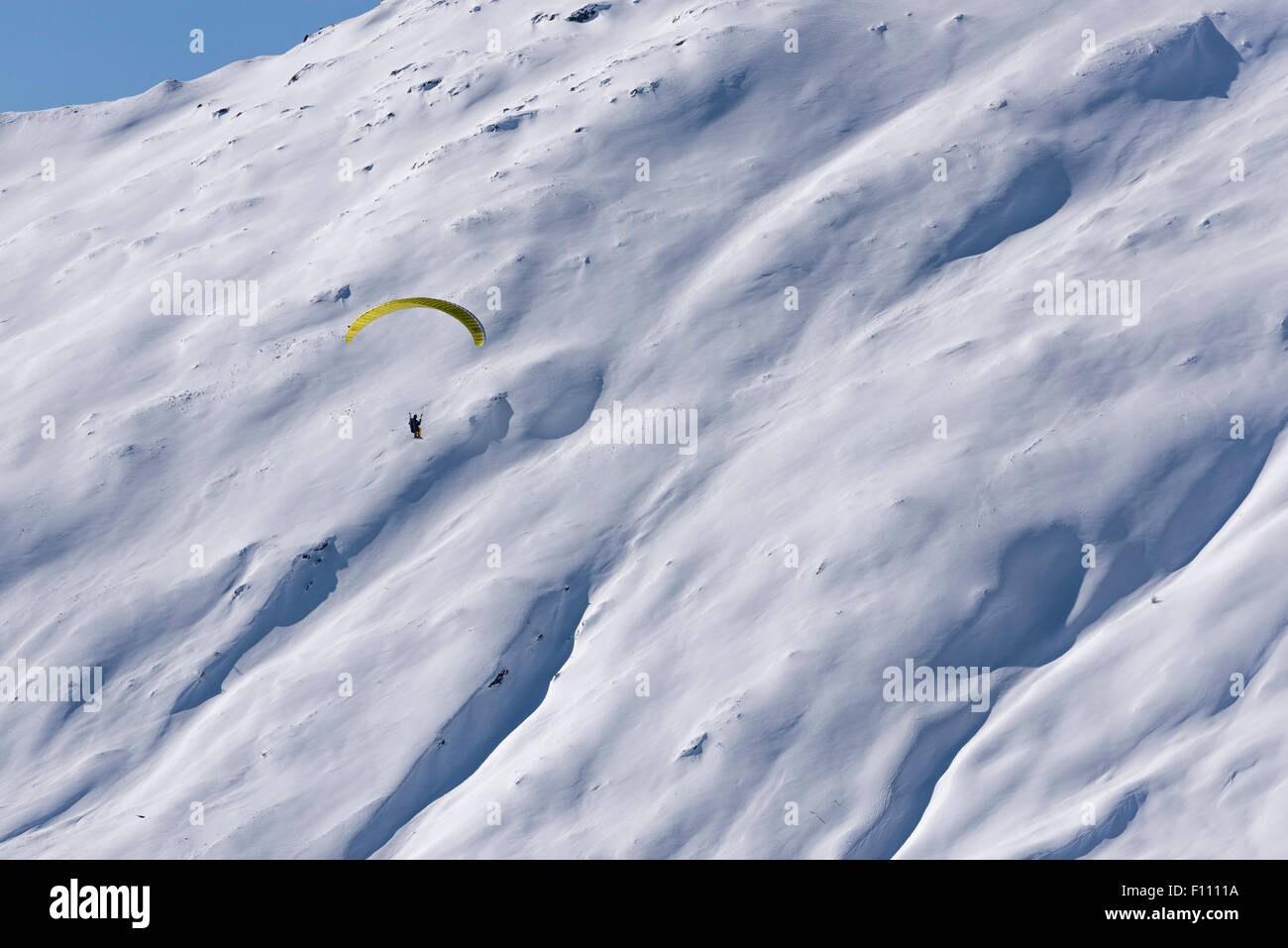 A paraglider is flying high up in the snow covered mountains above a ...