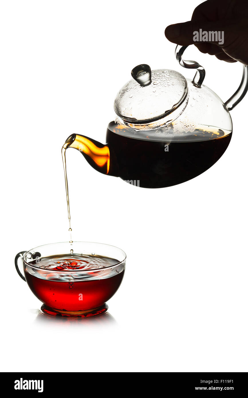 Frozen action of tea pouring from glass teapot to a glass mug. Backlit ...