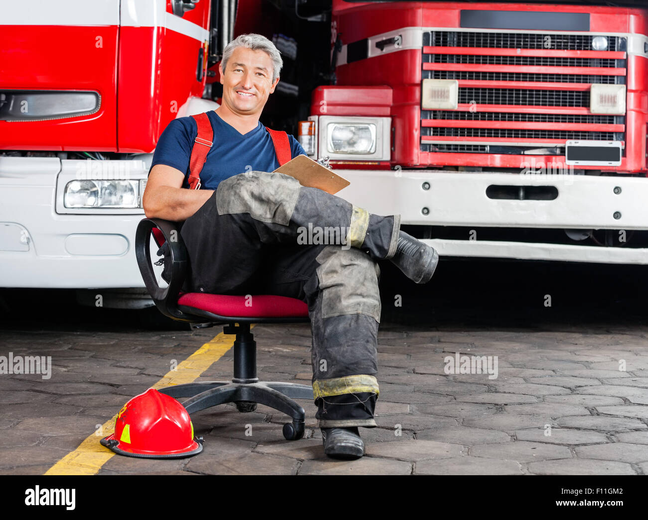 Happy Firefighter Sitting On Chair Against Trucks Stock Photo - Alamy