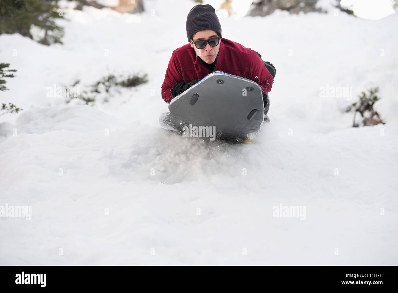 Hispanic man sledding on snowy hillside Stock Photo - Alamy