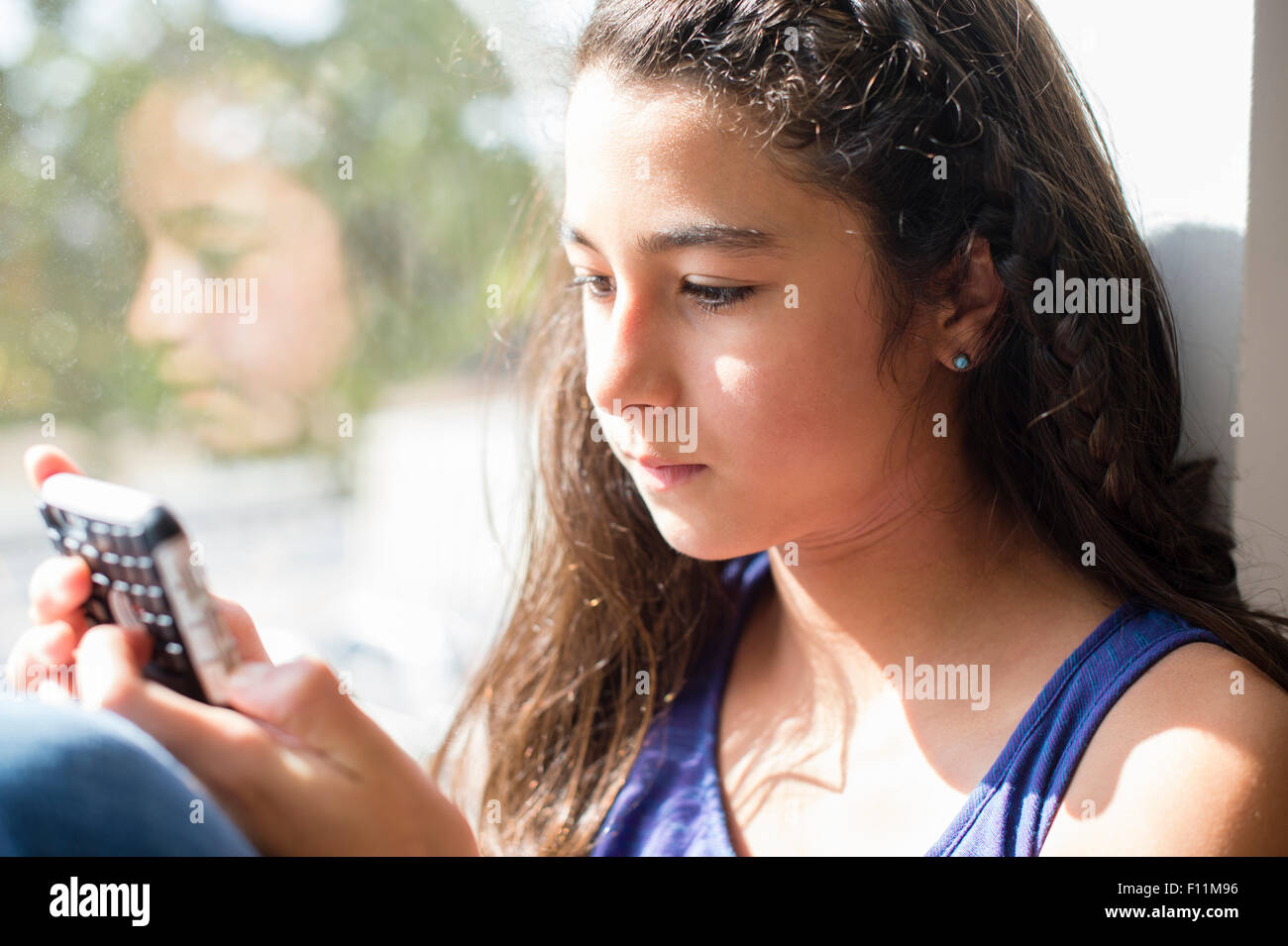 Mixed race girl using cell phone at window Stock Photo - Alamy