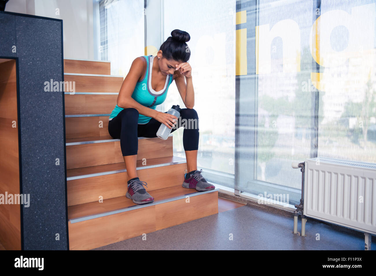 Tired woman sitting on the stairs with bottle of water in gym Stock ...