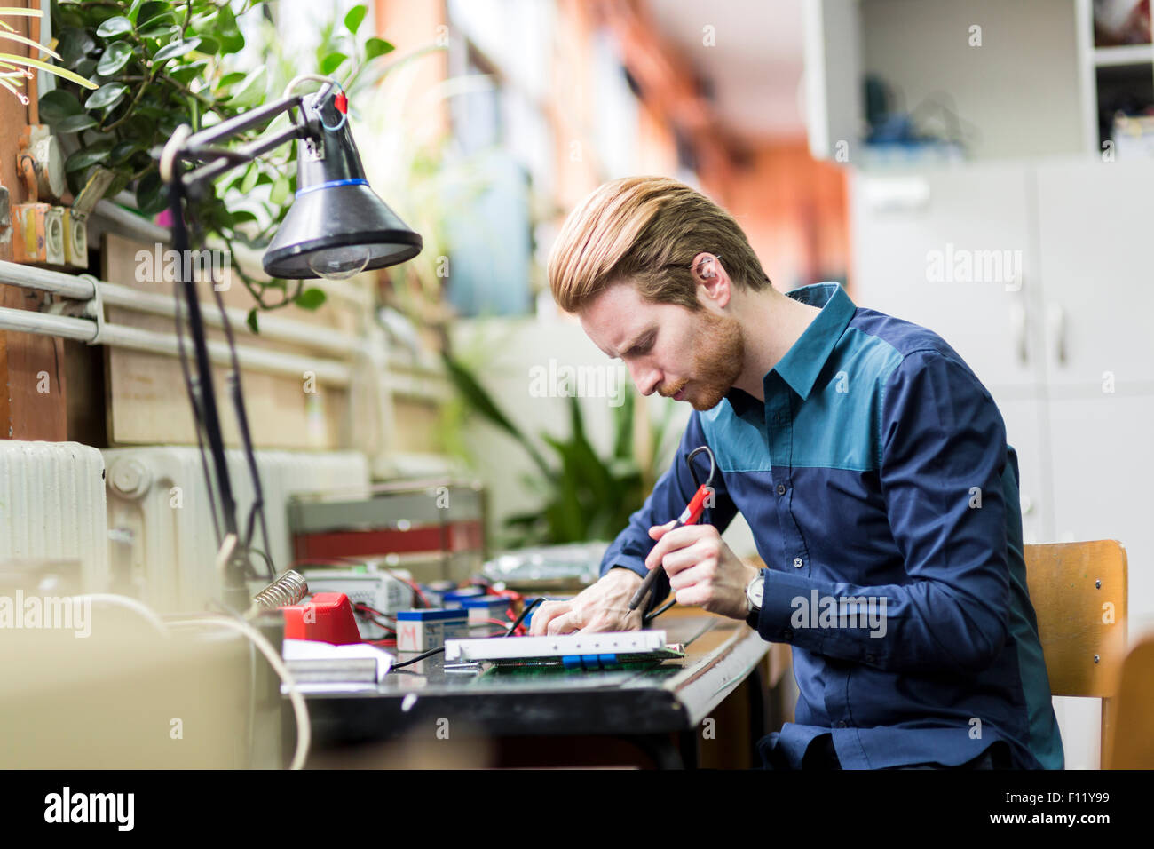 Young handsome man soldering a circuit board and working on fixing ...