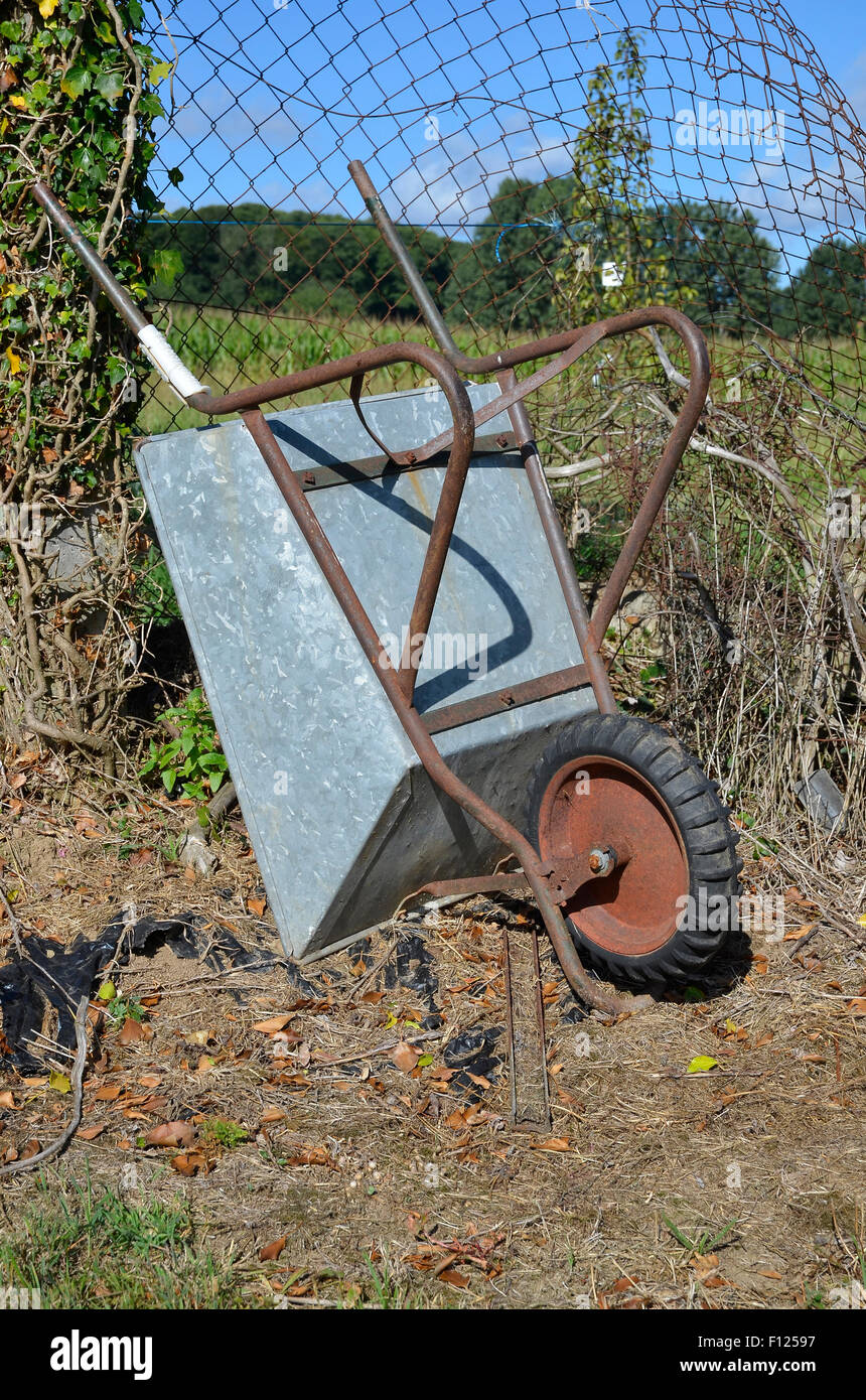 Galvanised steel wheel barrow leaning against a fence in a rural garden ...