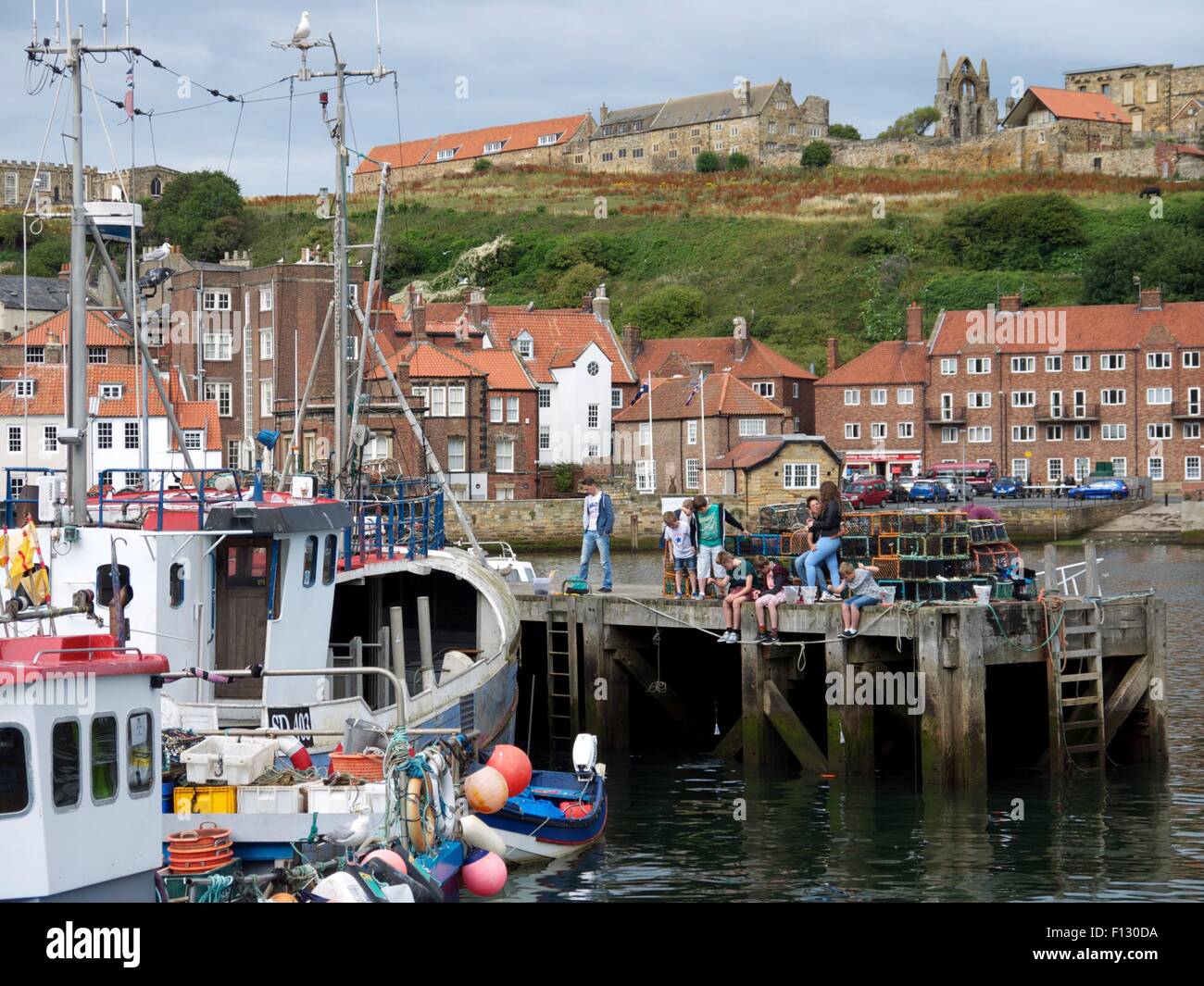 Whitby harbor with a fishing boat, tourists crab fishing and the church ...