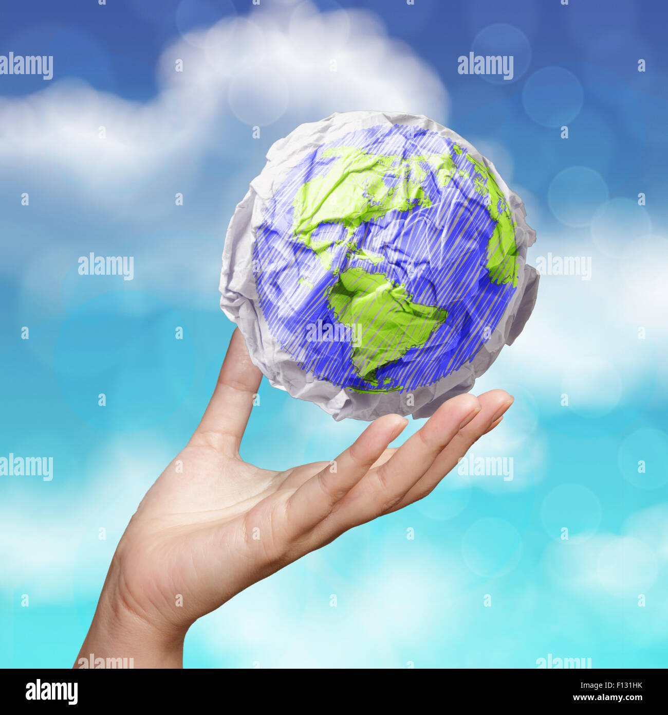 hand showing crumpled world paper symbol as concept on blue sky ...
