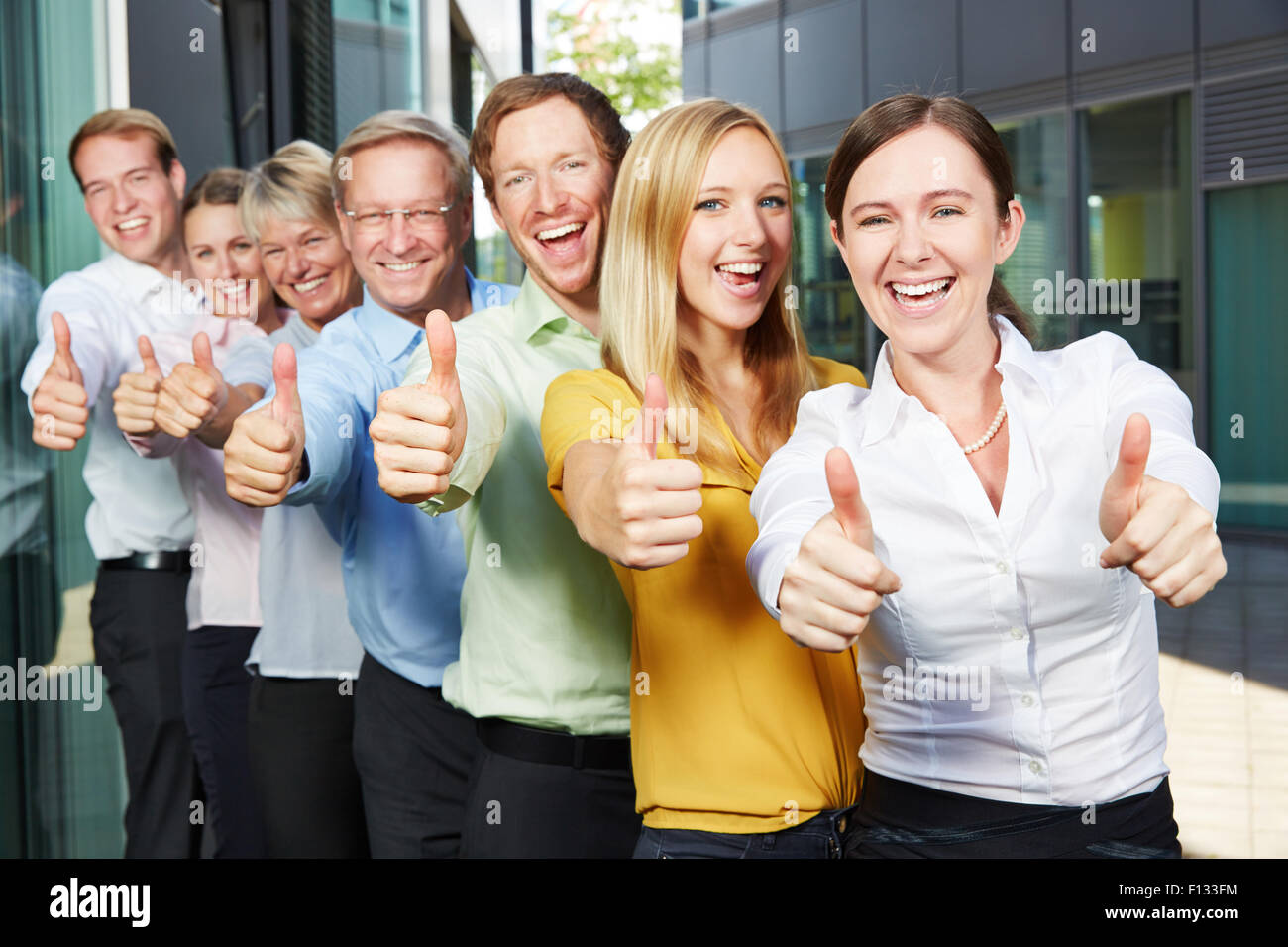 Cheering business people team holding thumbs up next to the office ...