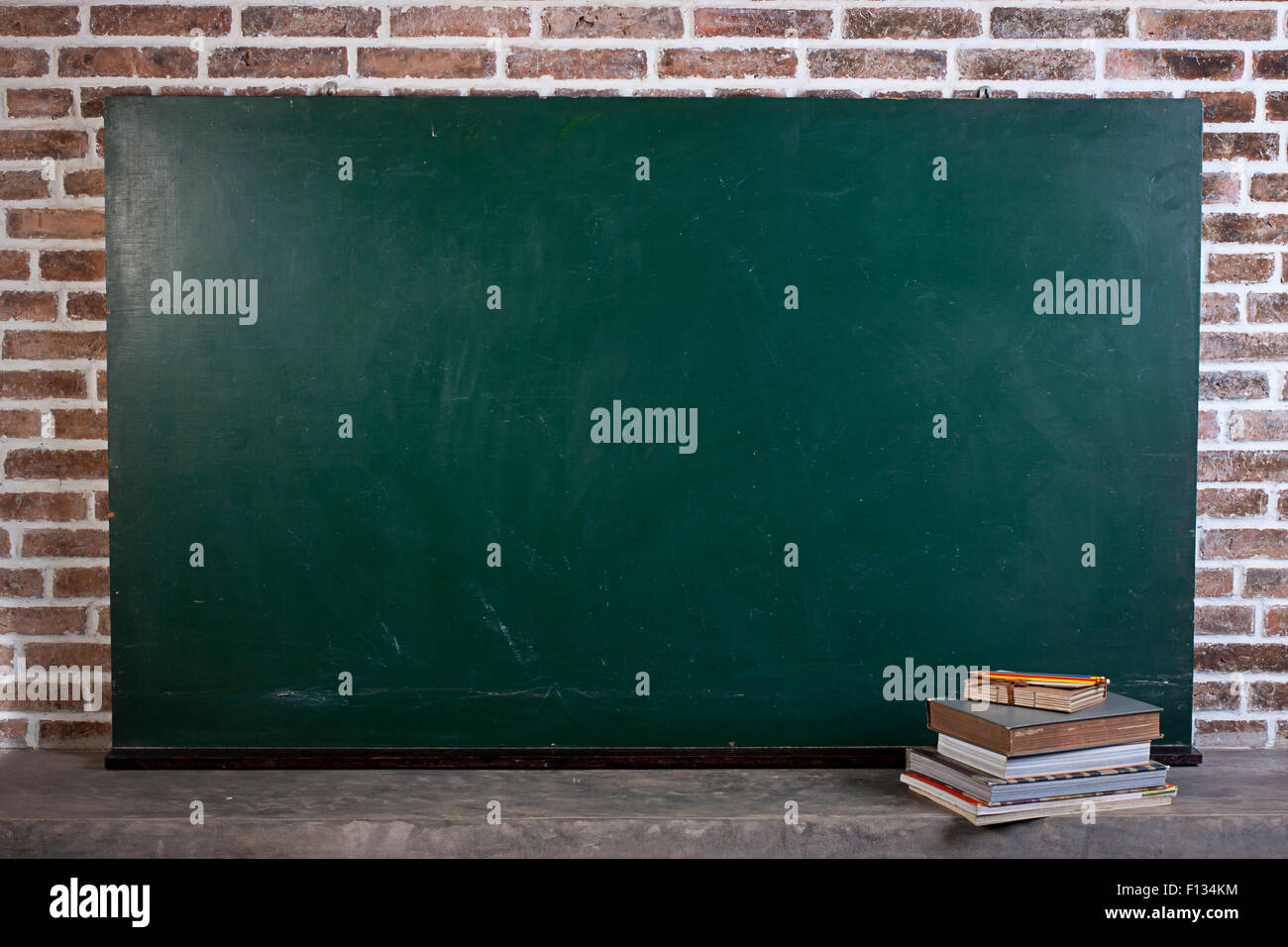 Green chalkboard with stack of books on a brick wall Stock Photo - Alamy