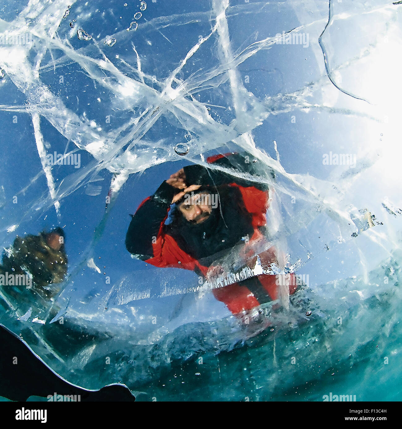 Man looking through transparent ice (1m thick) on lake surface to see ...