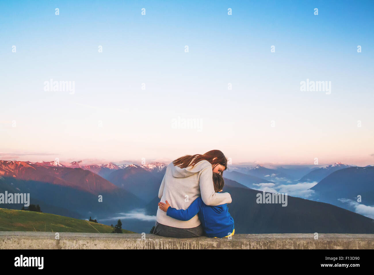 Rear view of woman sitting on a wall hugging her son Stock Photo - Alamy