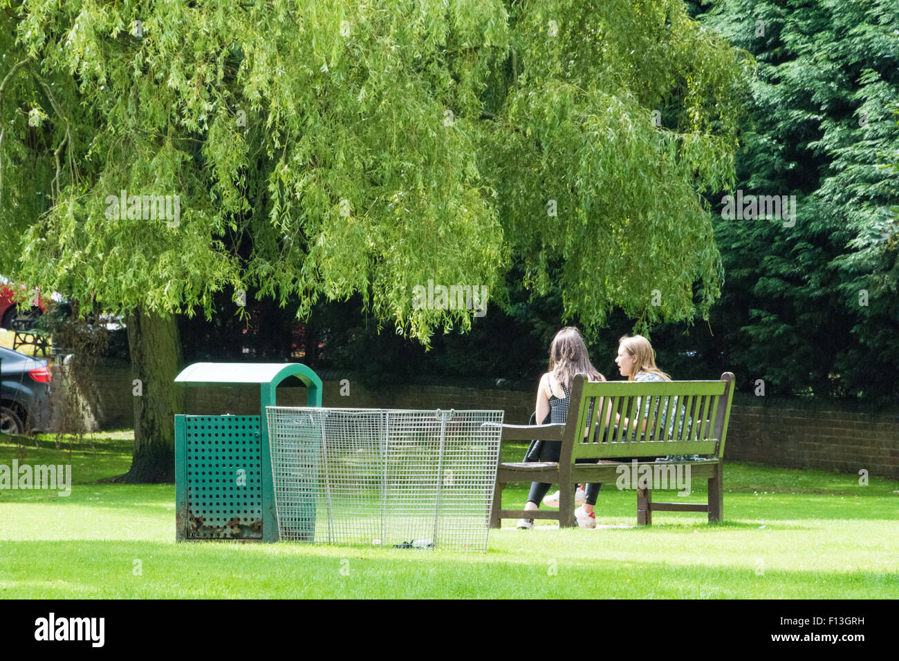 Two young girls sitting on a bench at Tettenhall Pool Wolverhampton UK ...