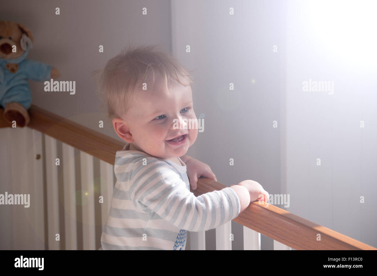 Baby boy in nursery waking up in his white cot with teddy in the ...