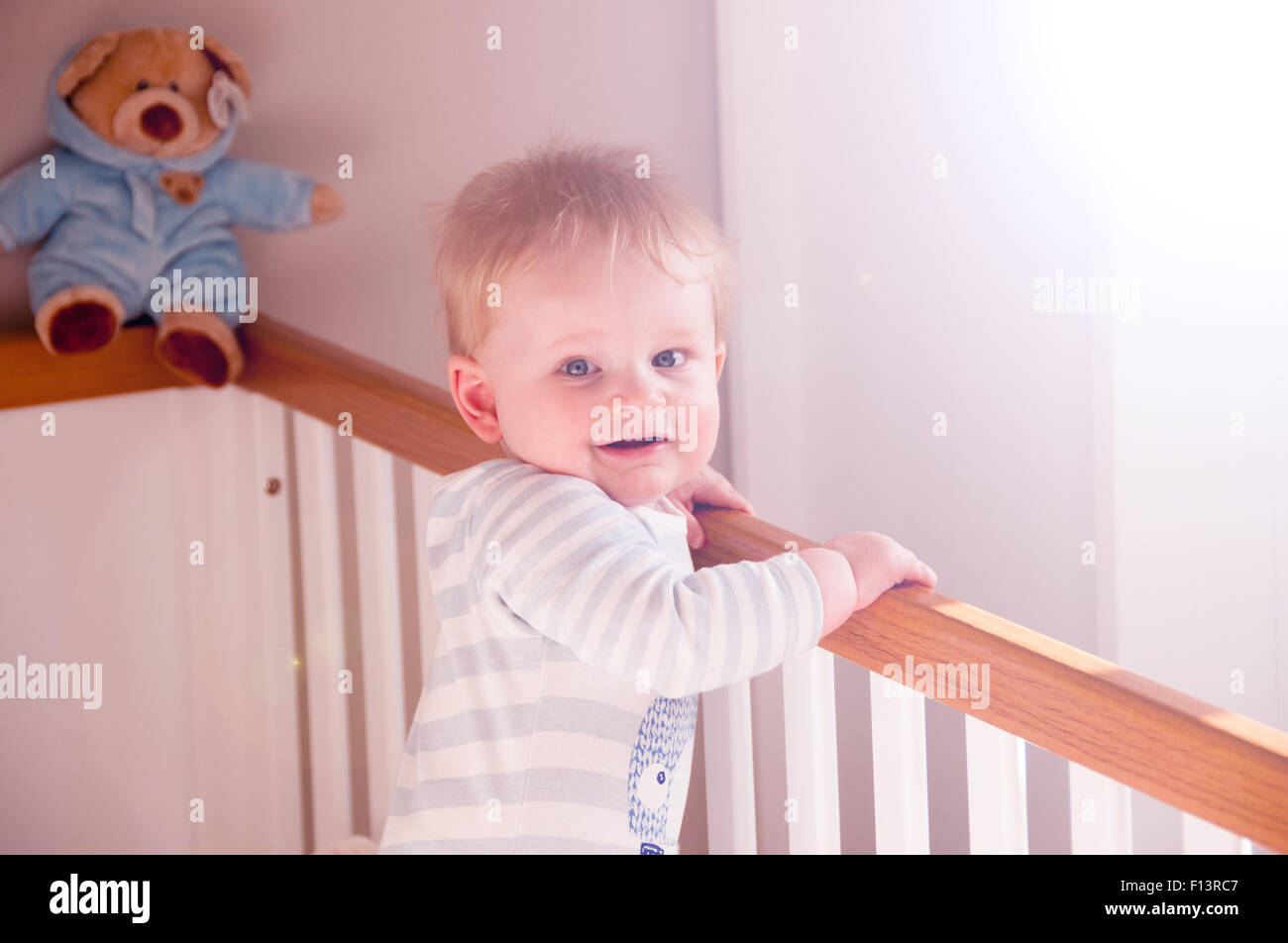Baby boy in nursery waking up in his white cot with teddy in the ...