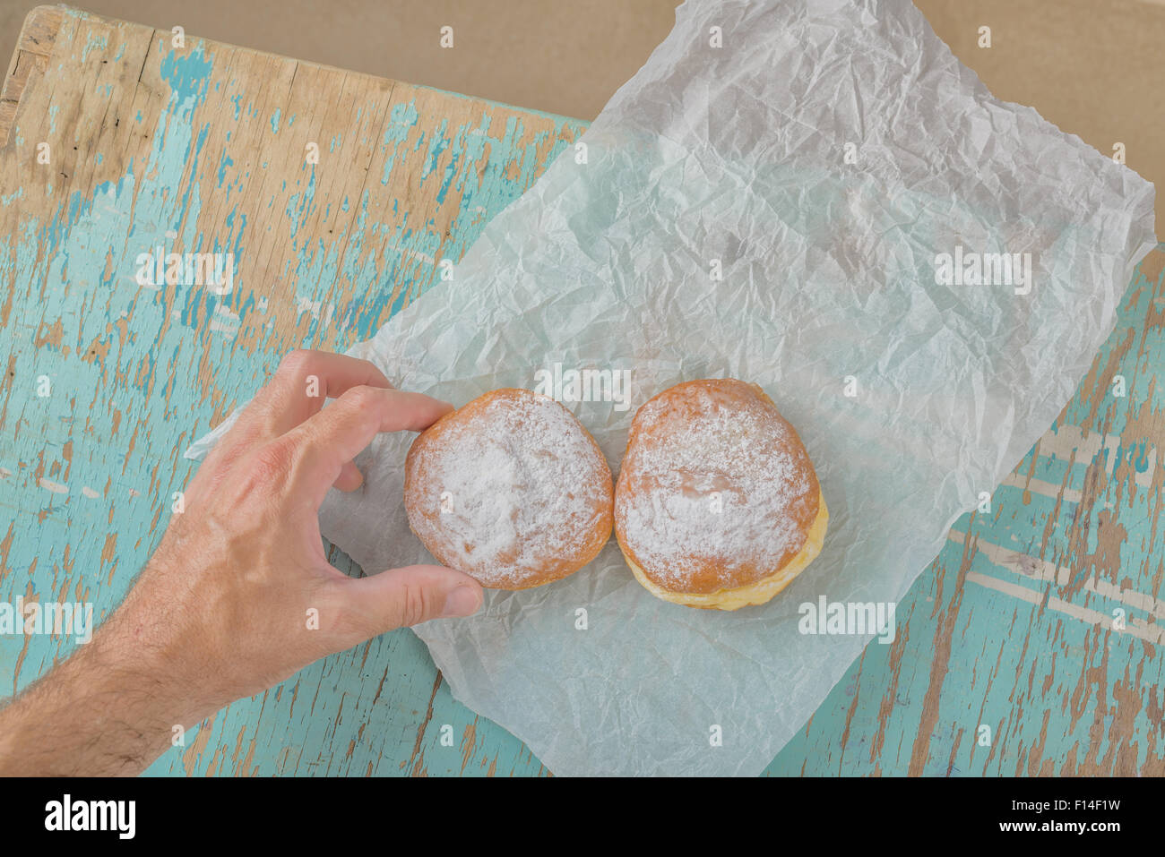Male hand reaches and taking sweet sugary donut from rustic wooden ...