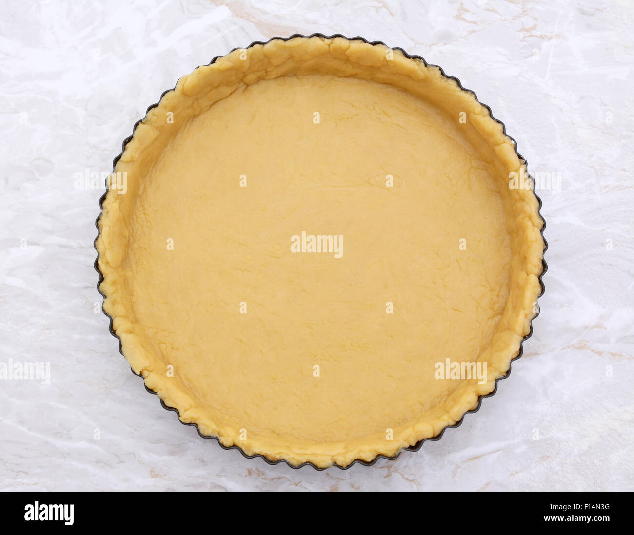 Circular metal flan tin lined with shortcrust pastry on a kitchen work ...
