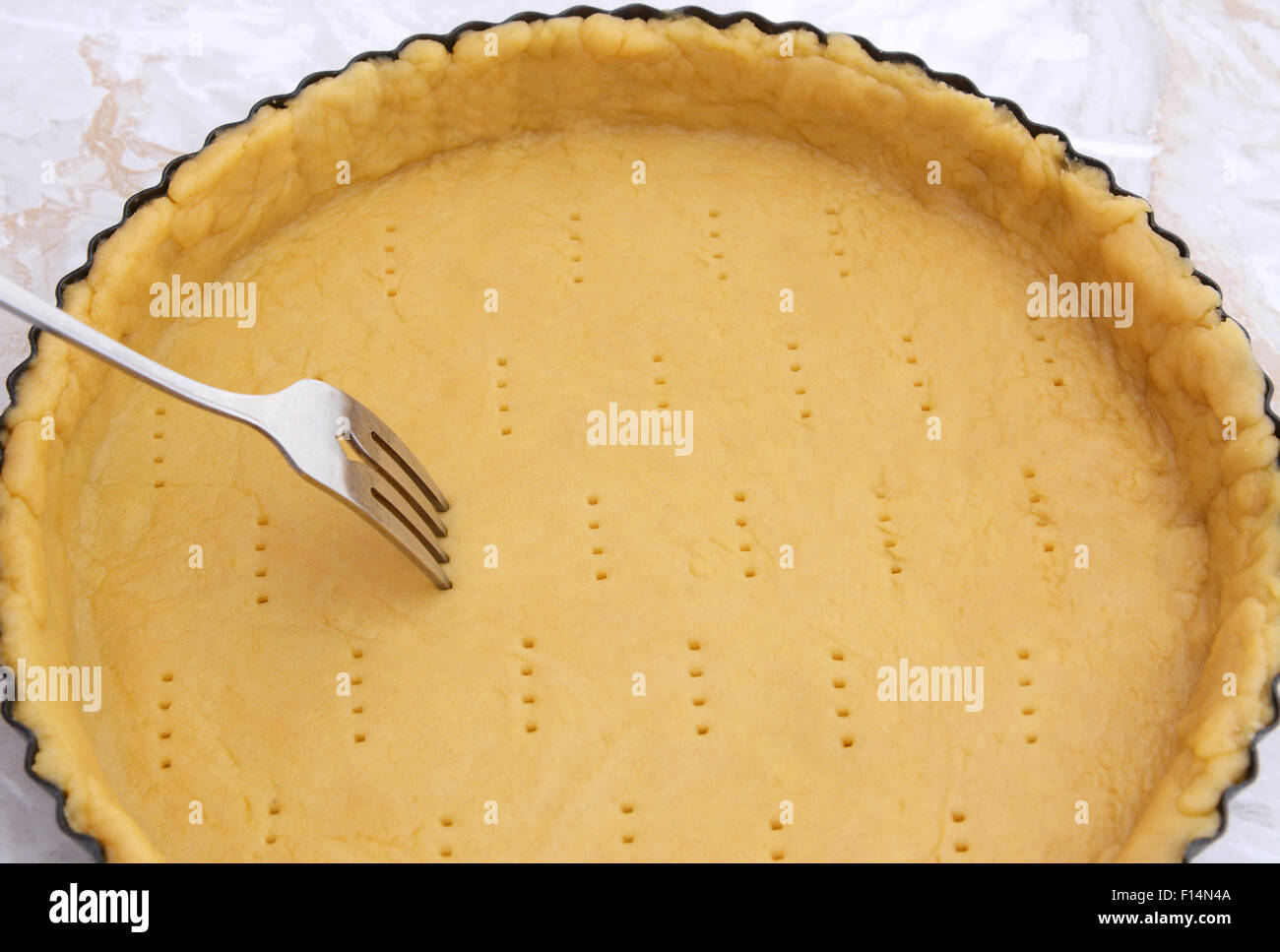 Metal fork makes holes in a raw pastry case in a metal baking tin Stock ...