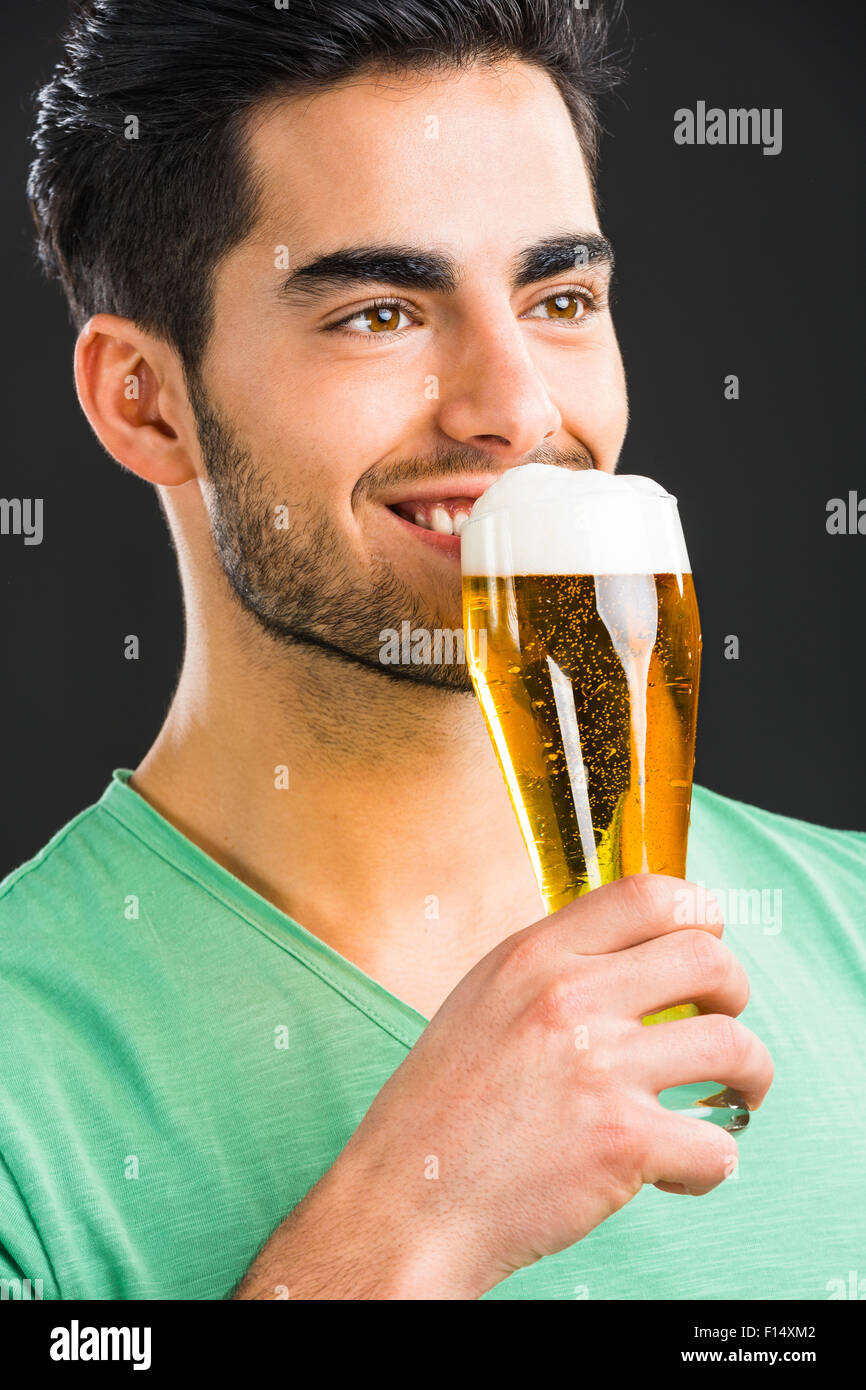 Portrait of handsome young man tasting a draft beer, isolated on gray ...