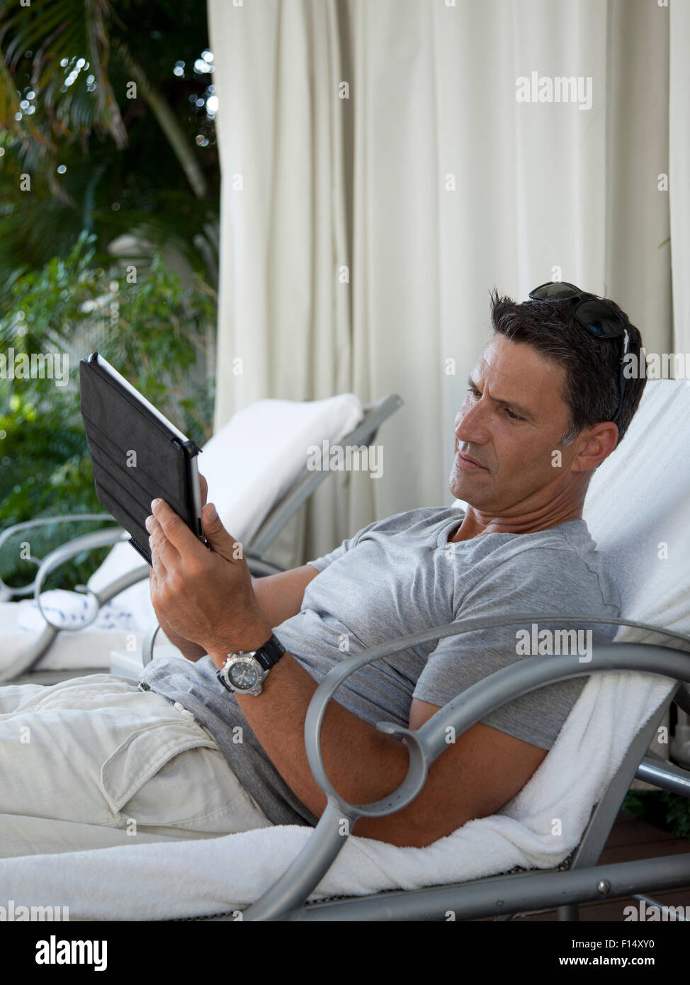 Man laying on lounge chair using digital tablet Stock Photo - Alamy