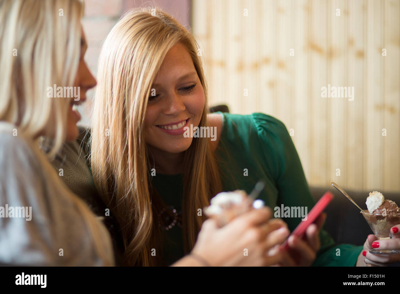 Women eating ice cream dessert and using cell phones on sofa Stock ...