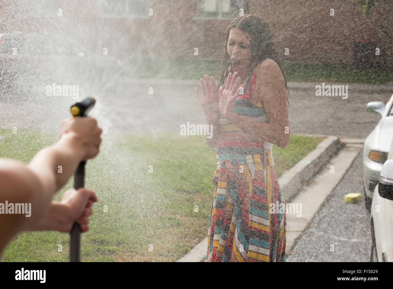 Hands spraying gasping woman with water hose by cars in suburban ...