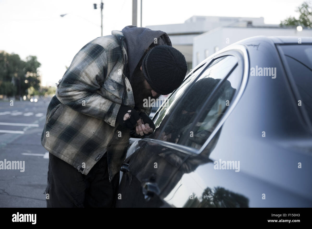USA, Utah, Salt Lake City, Homeless man breaking into car, side view ...