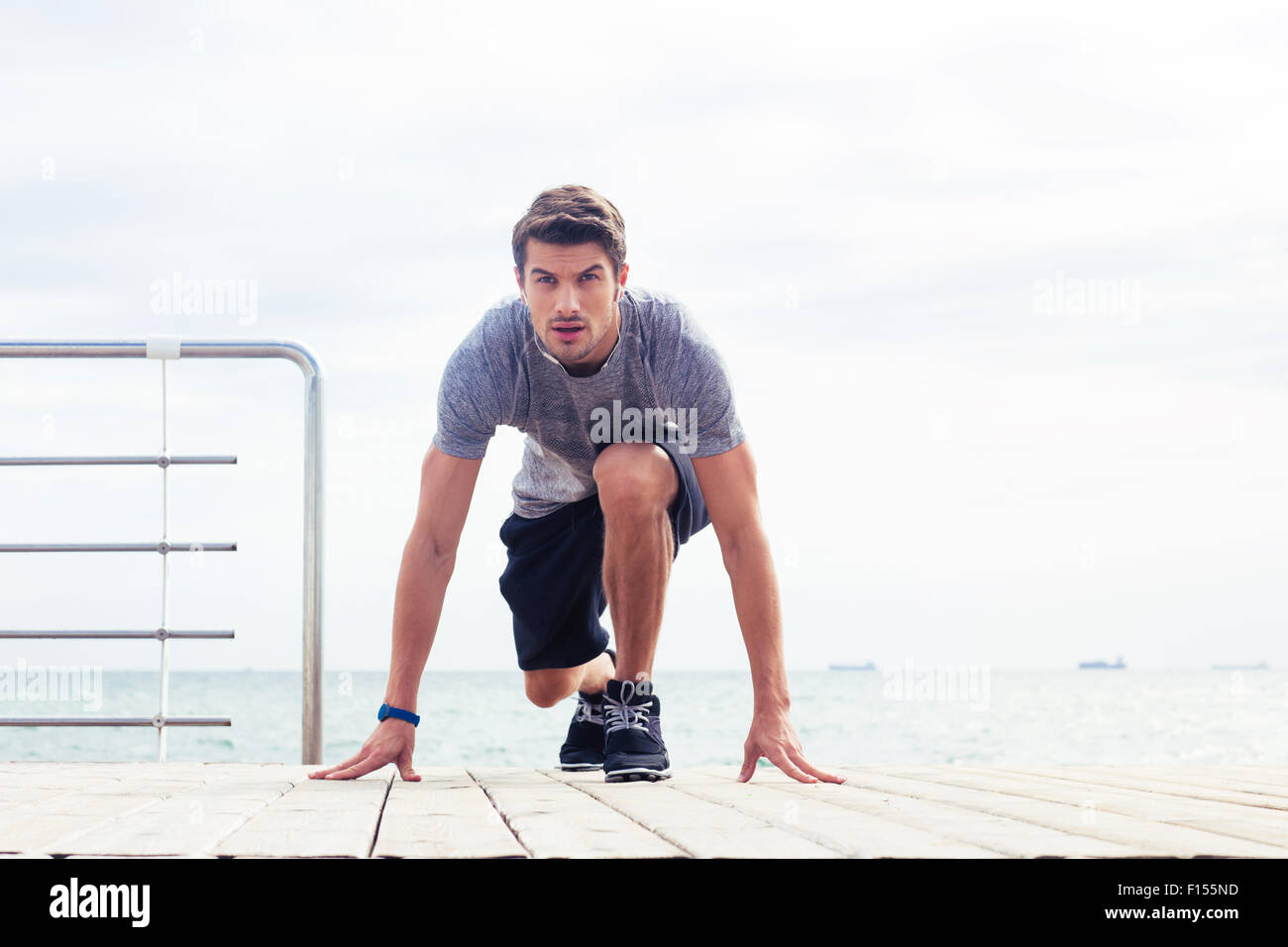 Portrait of a young male runner standing in start position outdoors ...