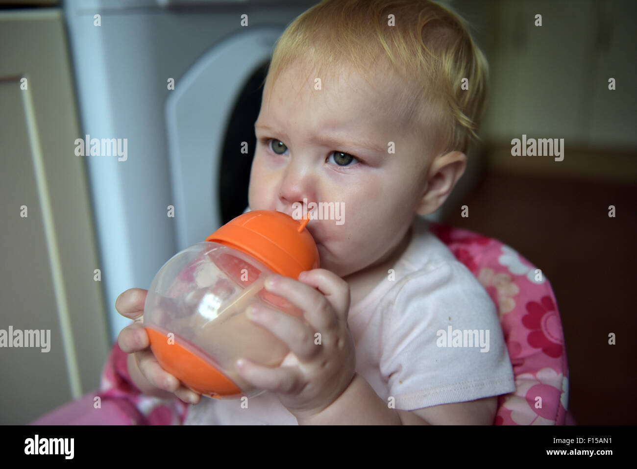 An eleven month old baby holding a bright orange beaker drinking water ...