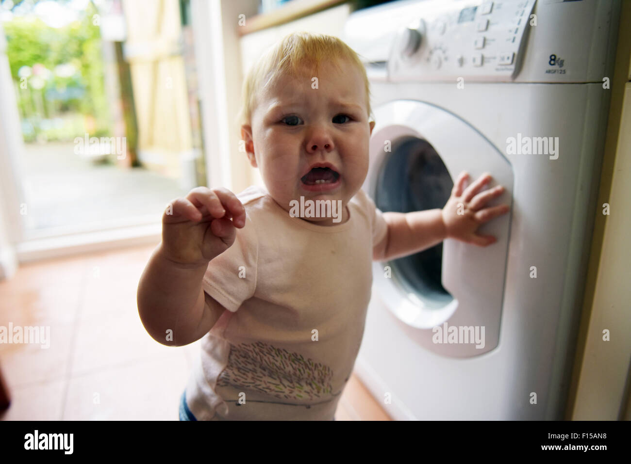 A teething eleven month old baby in the kitchen of her home crying with ...
