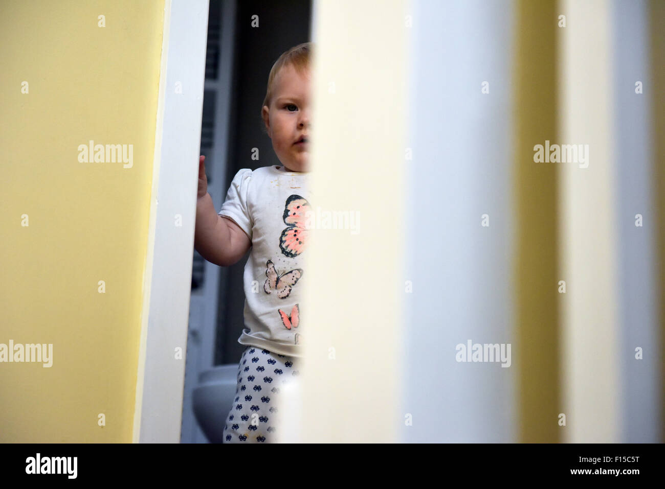 A one year old child standing alone at the top of a flight of stairs ...