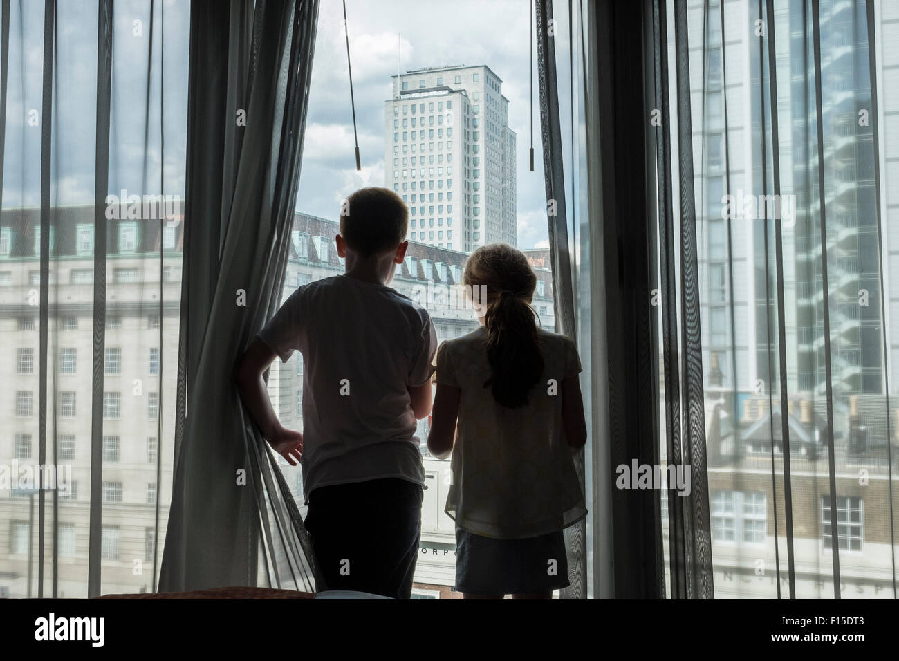Two children looking out of a window Stock Photo - Alamy